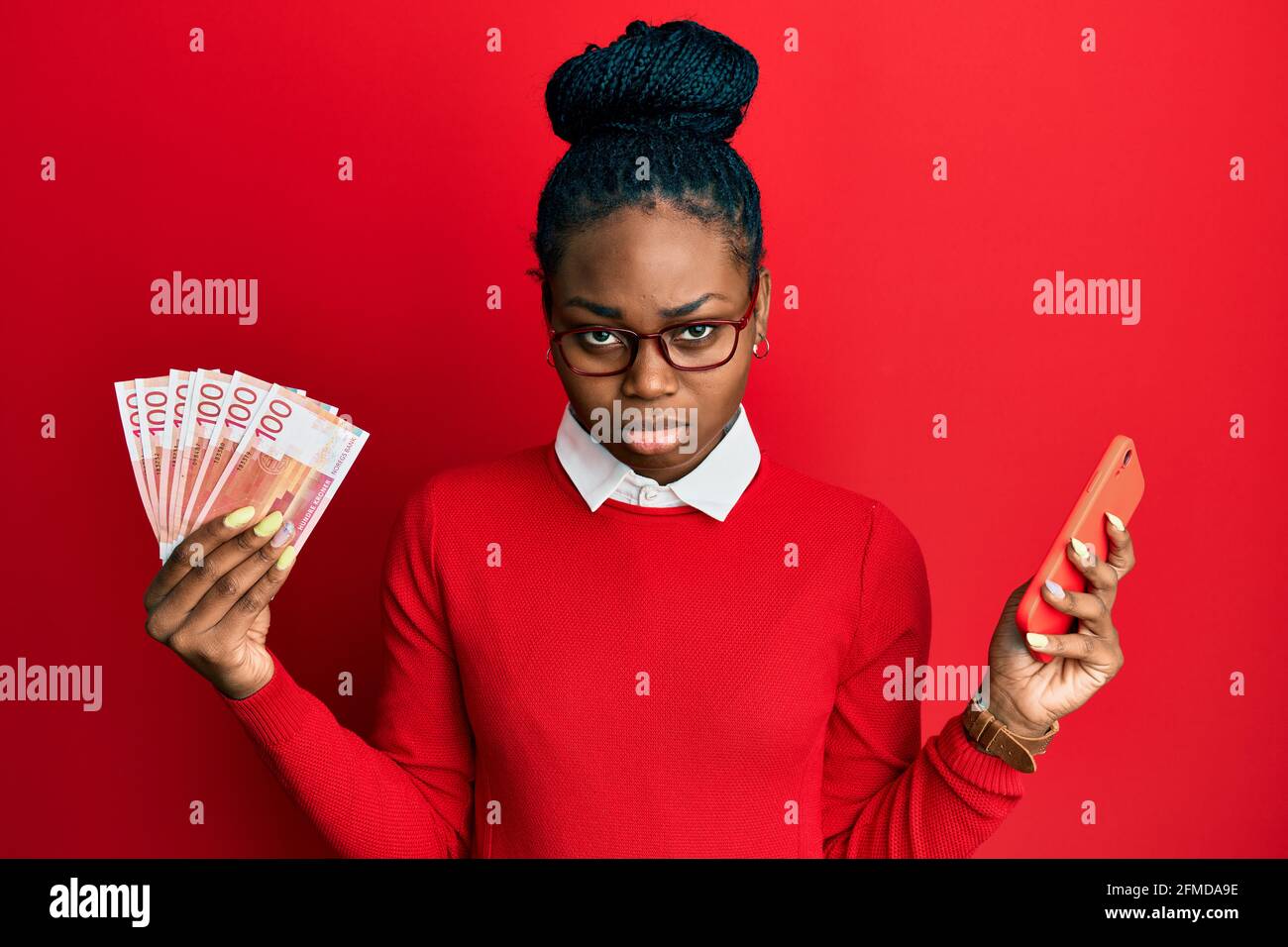 Young african american woman using smartphone holding norwegian krone ...