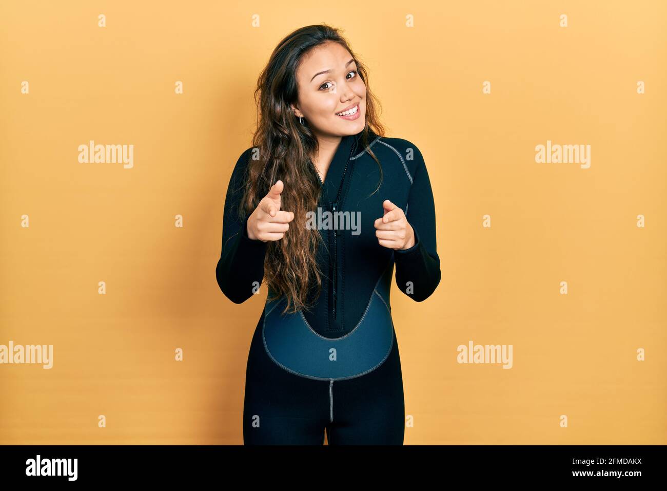 Young hispanic girl wearing diver neoprene uniform pointing fingers to ...