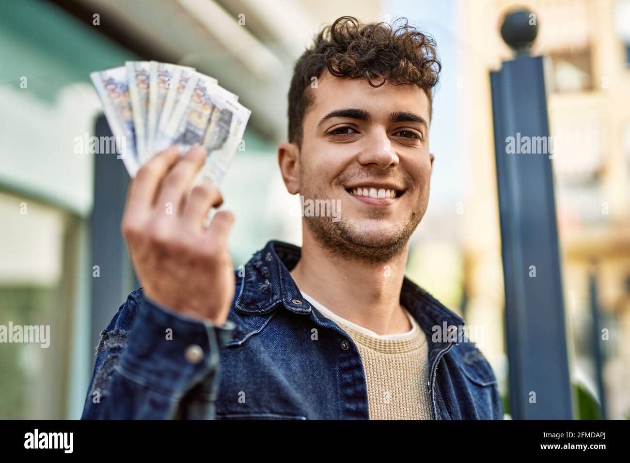Young hispanic man smiling happy holding peruvian sol banknotes at the ...