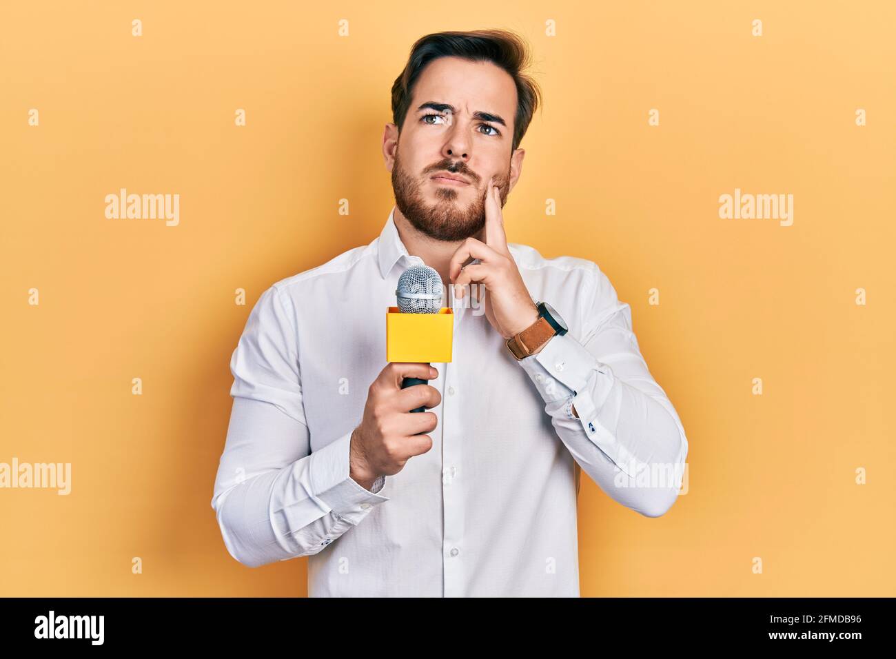 Handsome caucasian man with beard holding reporter microphone serious ...