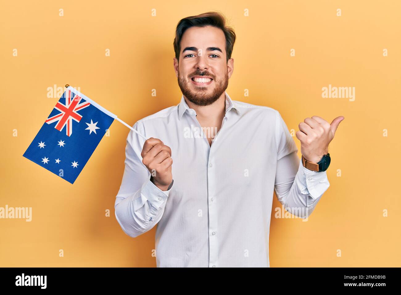 Handsome caucasian man with beard holding austria flag pointing thumb ...
