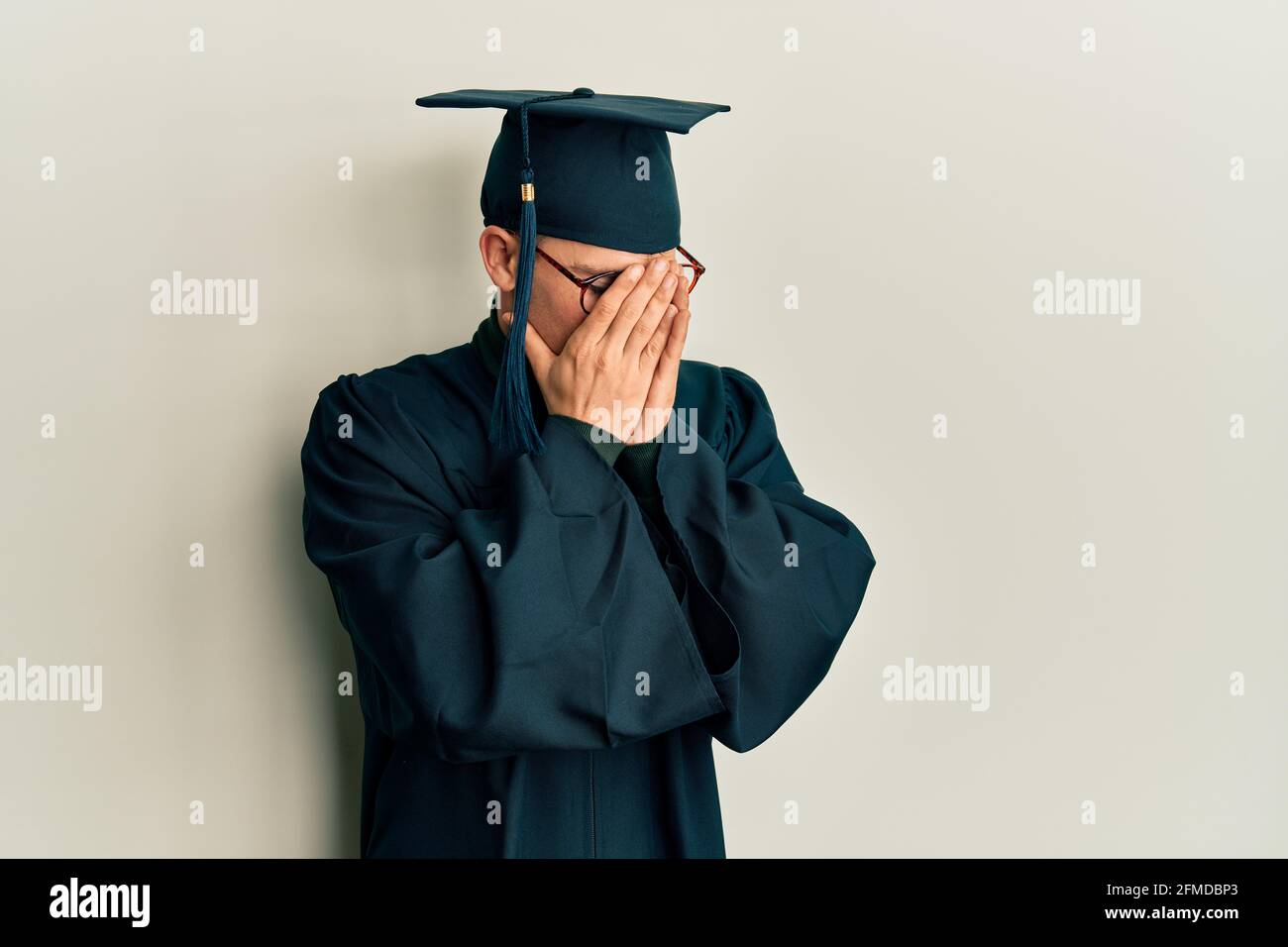 Young caucasian man wearing graduation cap and ceremony robe with sad ...