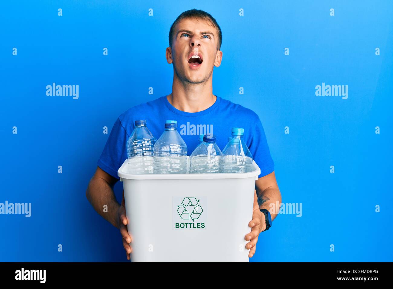 Young caucasian man holding recycling wastebasket with plastic bottles ...