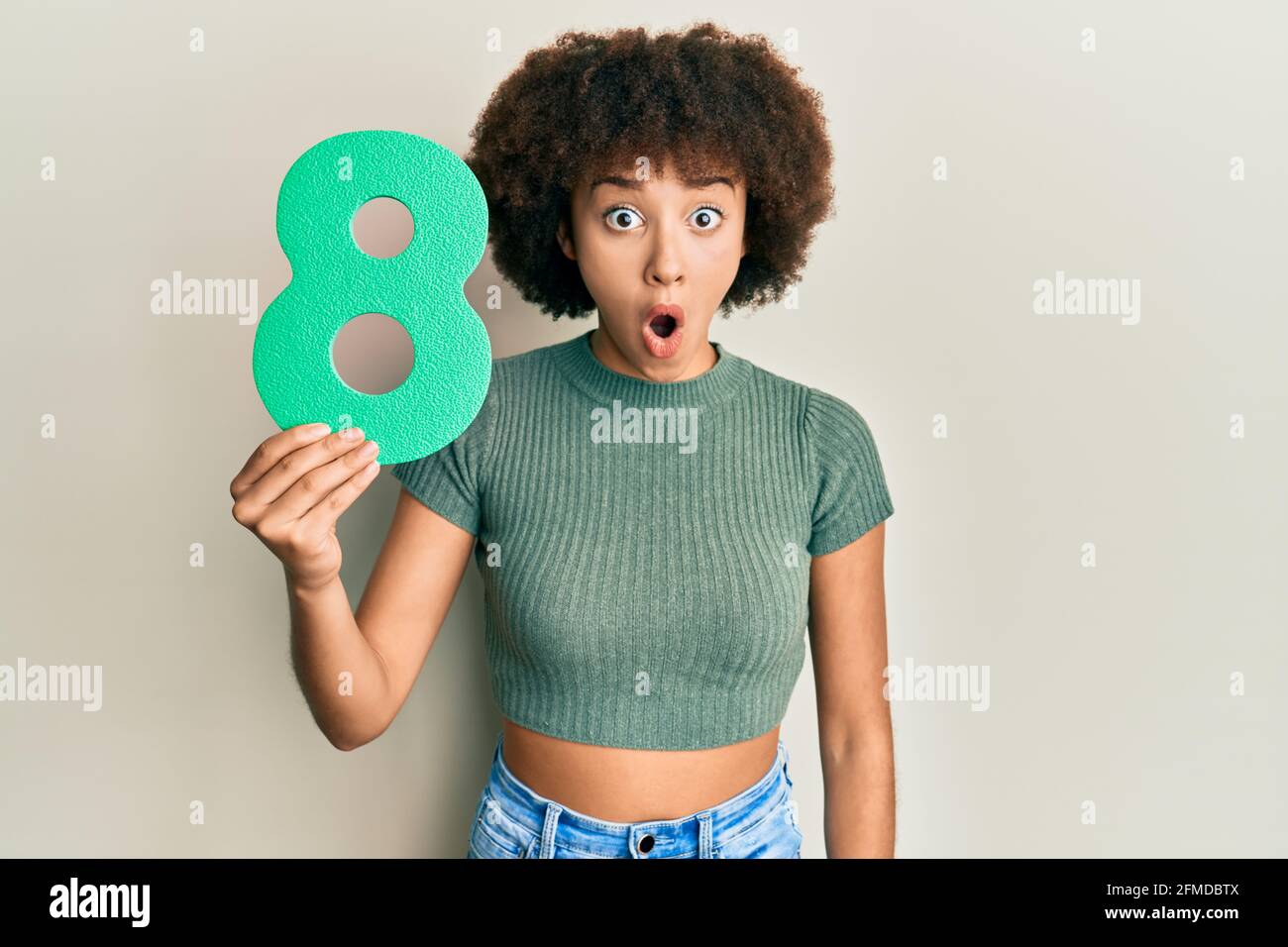 Young hispanic girl holding number eight scared and amazed with open ...