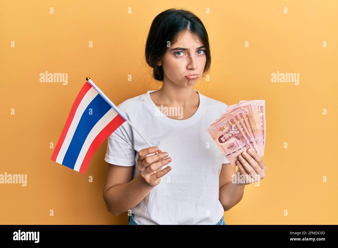 Young caucasian woman holding thailand flag and baht banknotes ...