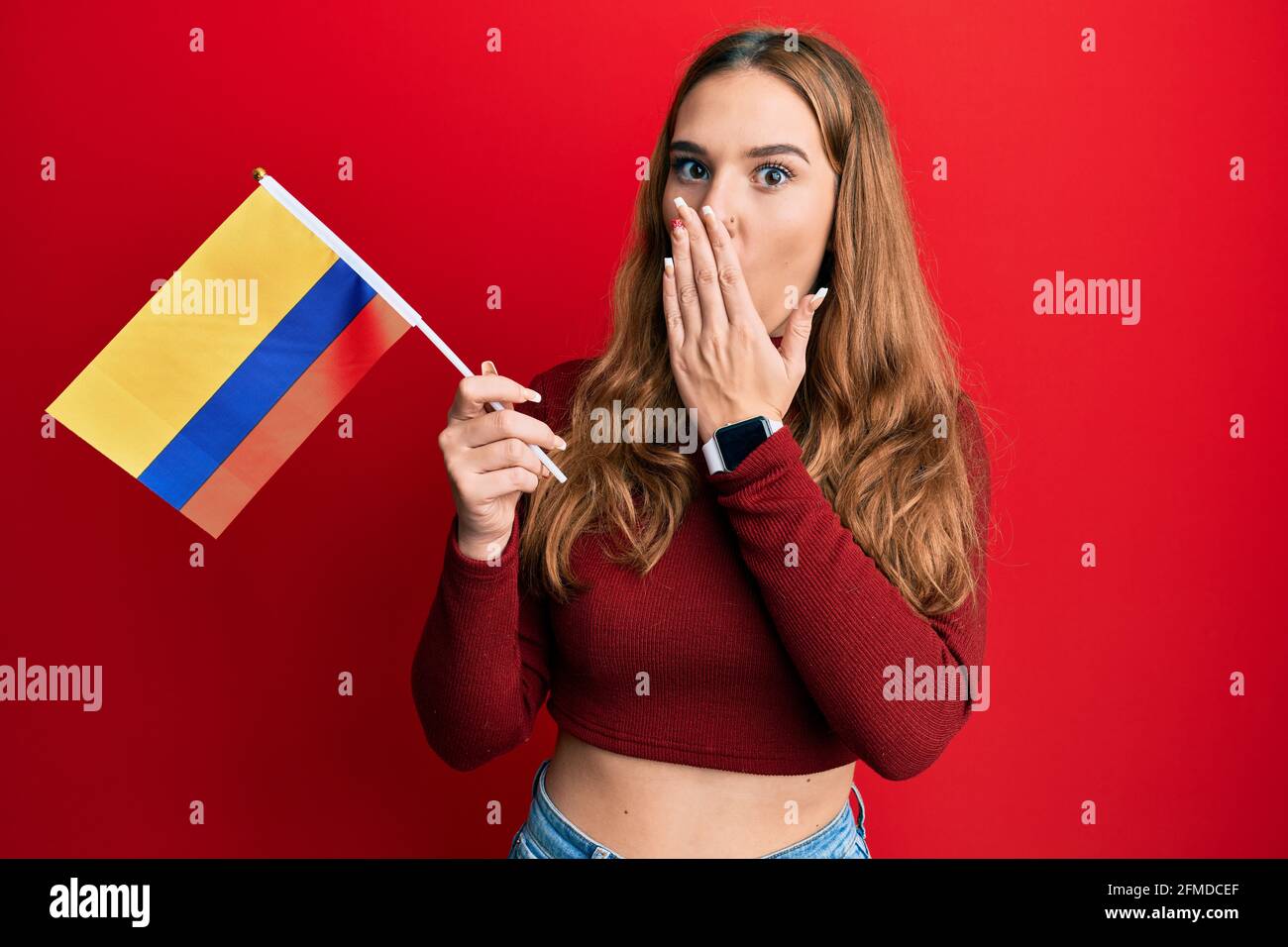 Young blonde woman holding colombia flag covering mouth with hand ...