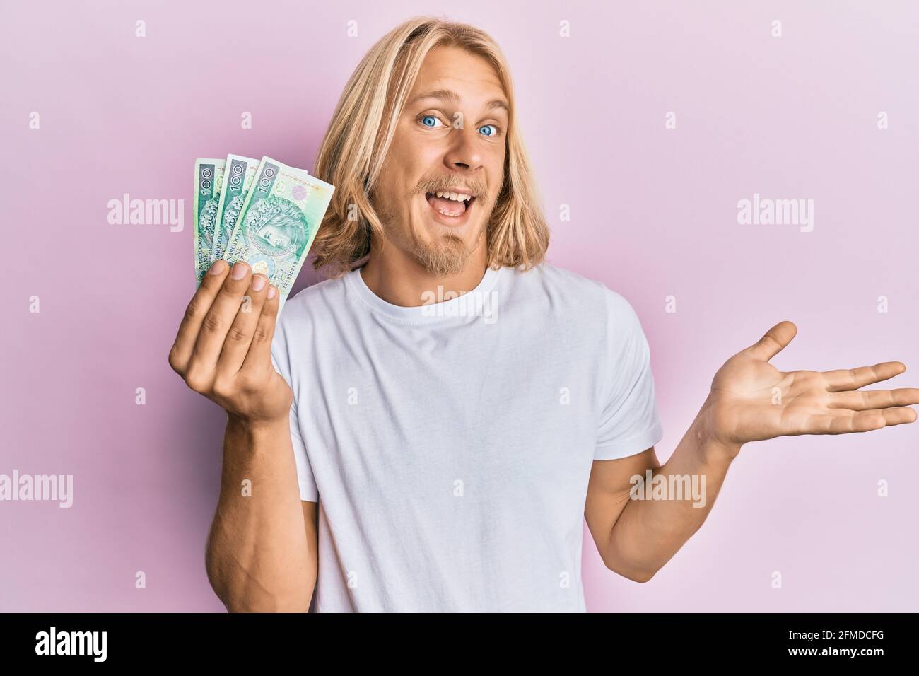 Caucasian young man with long hair holding 100 polish zloty banknotes ...