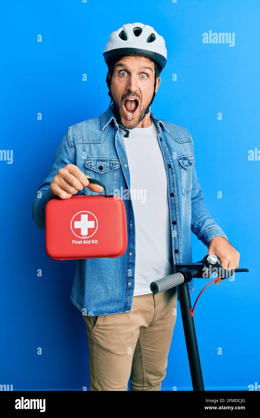 Young man standing on scooter wearing helmet holding first aid kit ...
