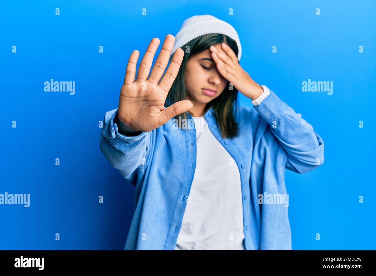 Young latin woman wearing cute wool cap covering eyes with hands and ...