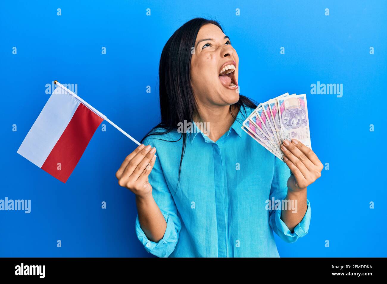 Young latin woman holding poland flag and zloty banknotes angry and mad ...
