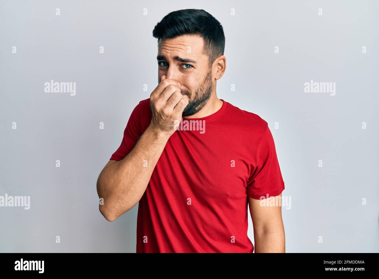 Young hispanic man wearing casual clothes smelling something stinky and ...
