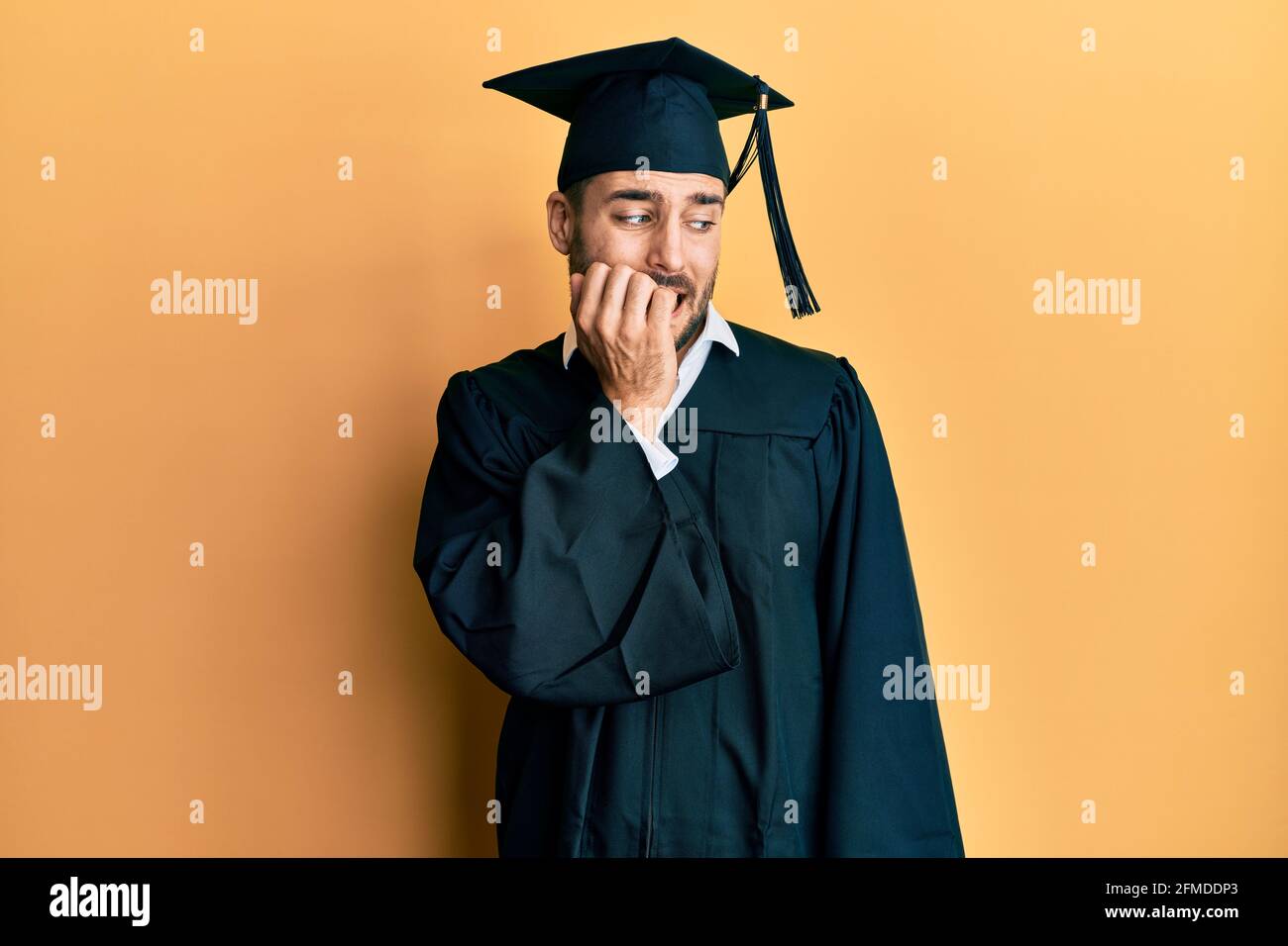 Young hispanic man wearing graduation cap and ceremony robe looking ...