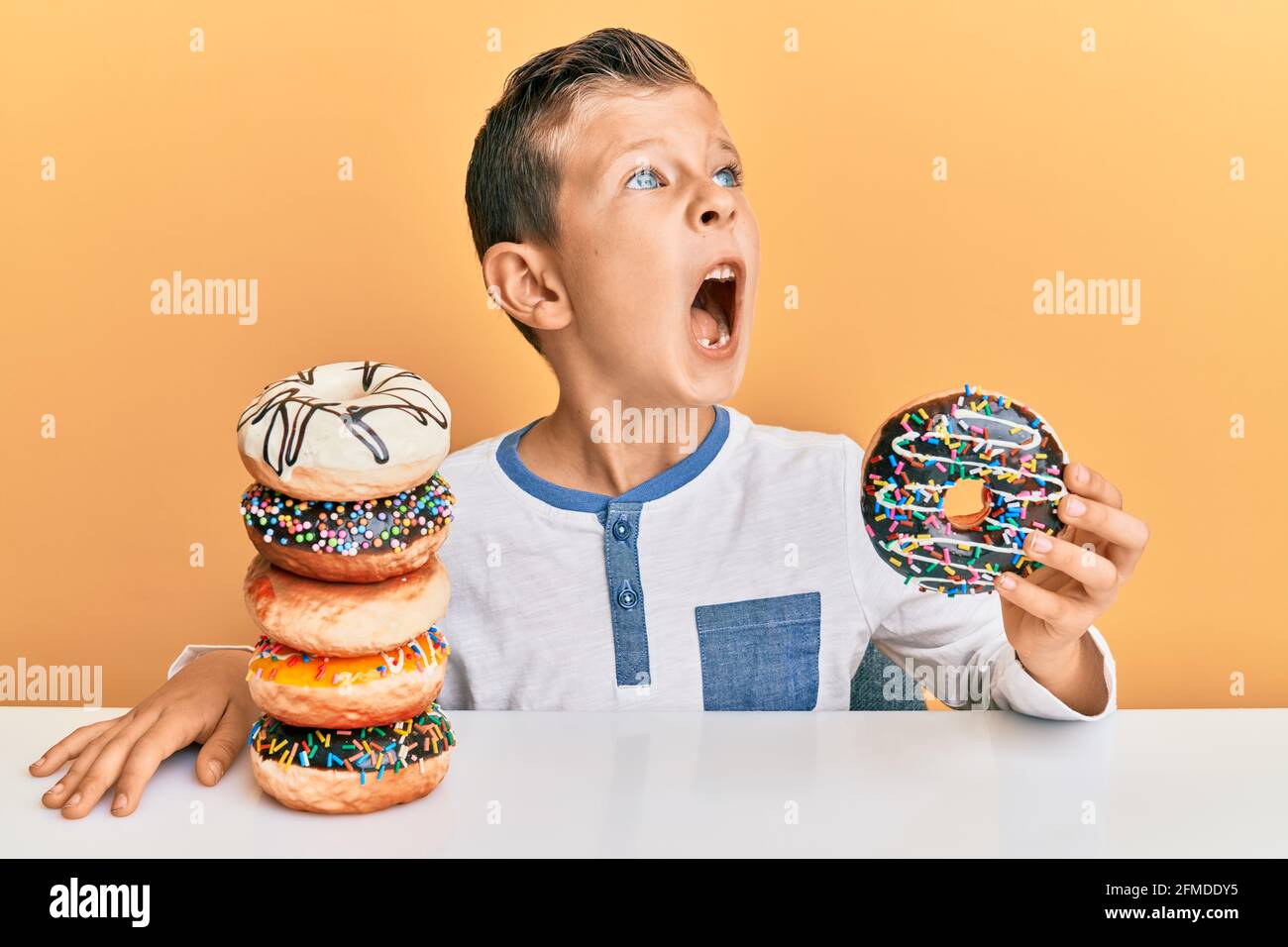 Adorable caucasian kid eating doughnuts for breakfast angry and mad ...