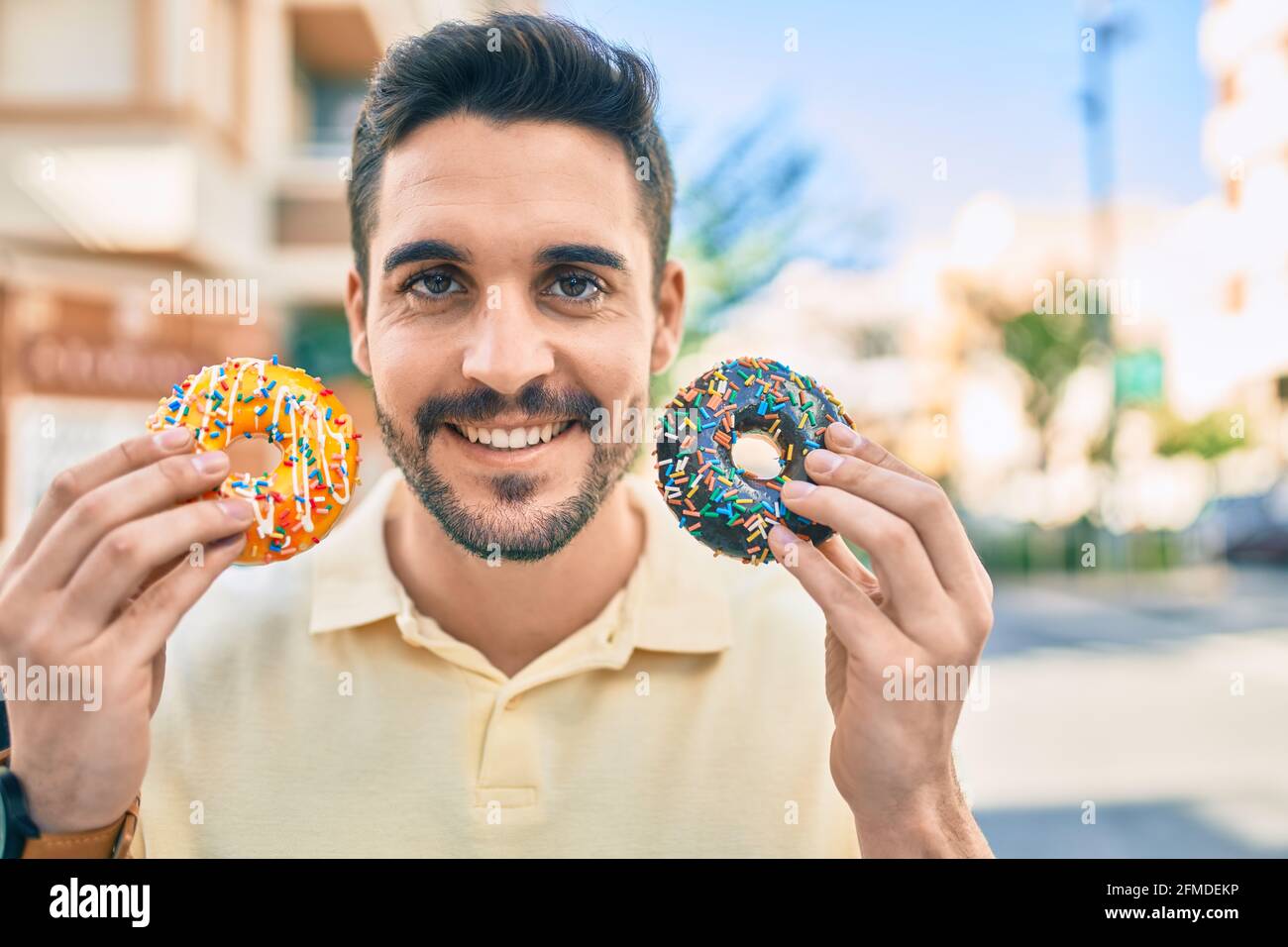 Young hispanic man smiling happy holding donuts walking at the city ...