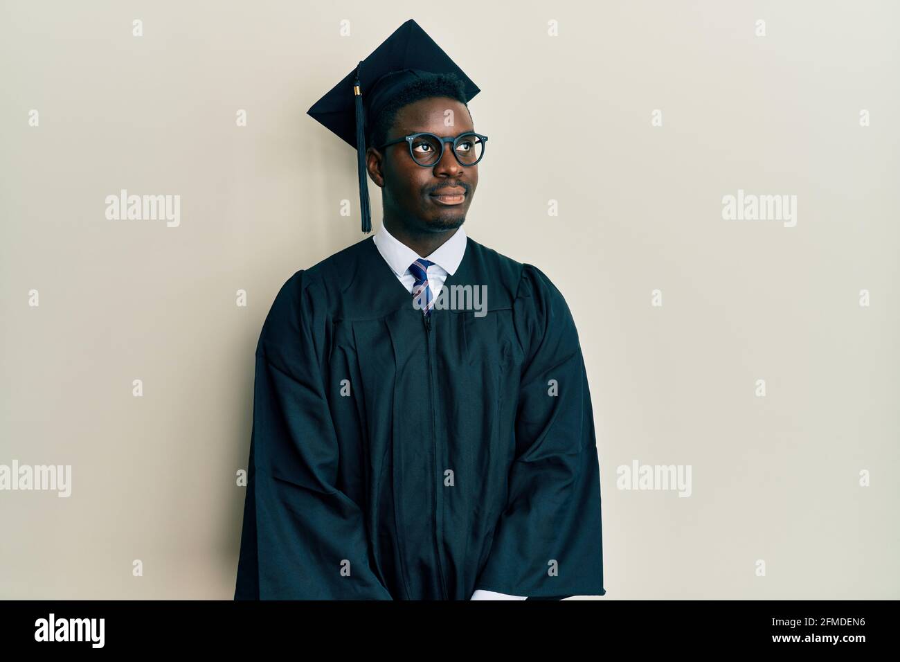 Handsome black man wearing graduation cap and ceremony robe smiling ...