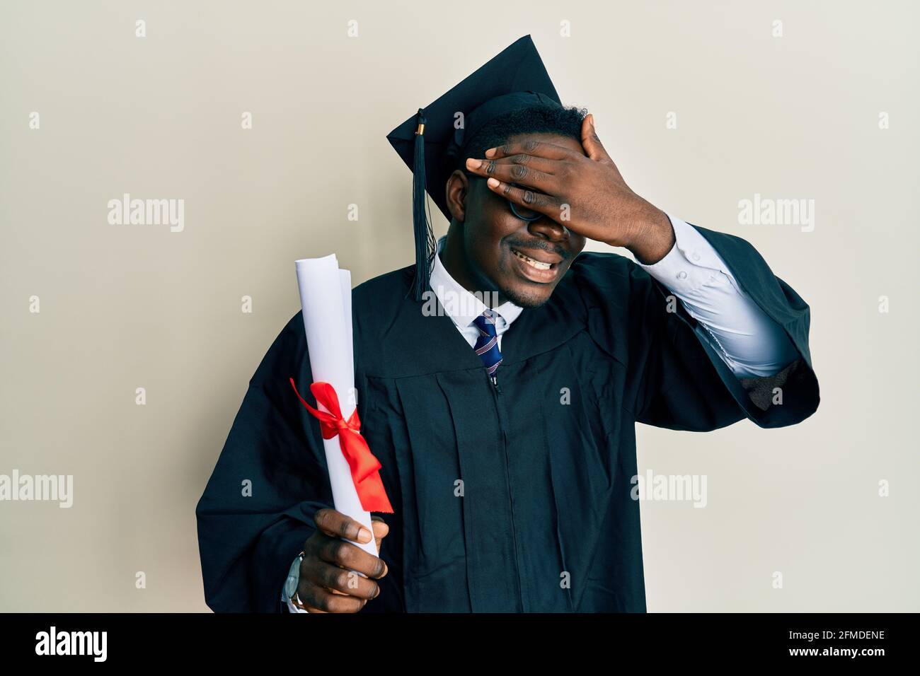 Handsome black man wearing graduation cap and ceremony robe holding ...