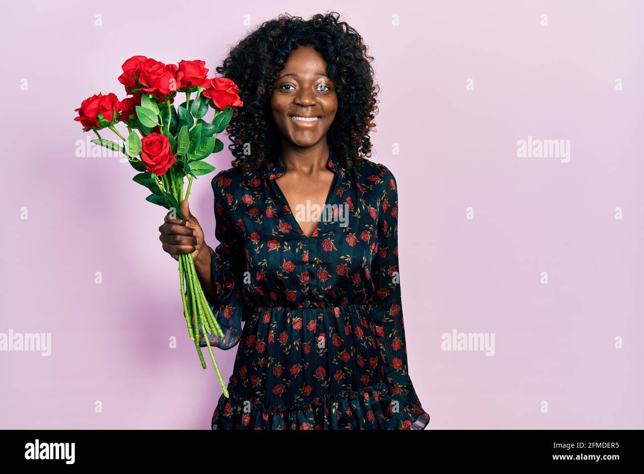 Young african american woman holding bouquet of red roses looking ...