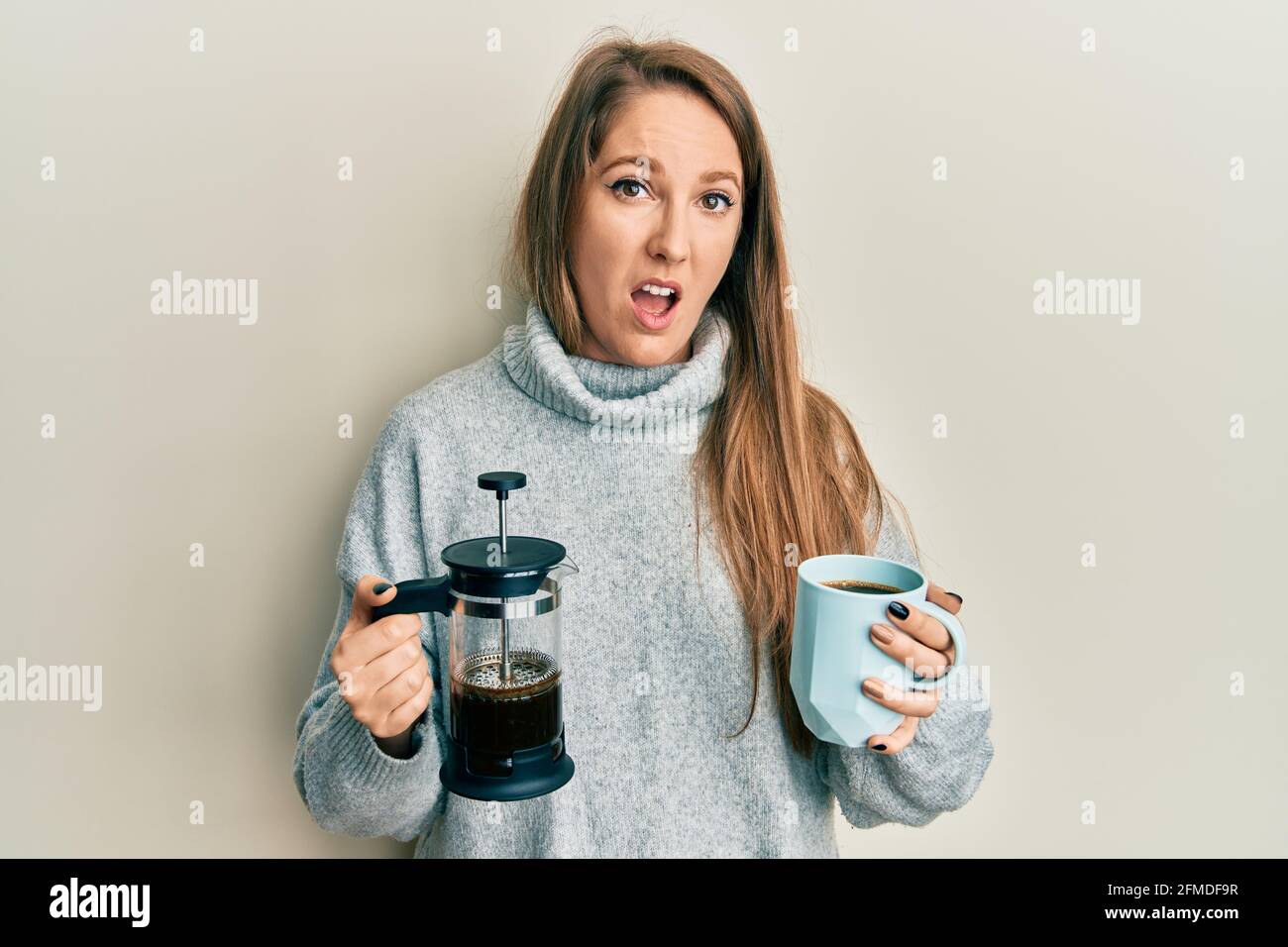 Young blonde woman drinking a cup of italian coffee in shock face ...