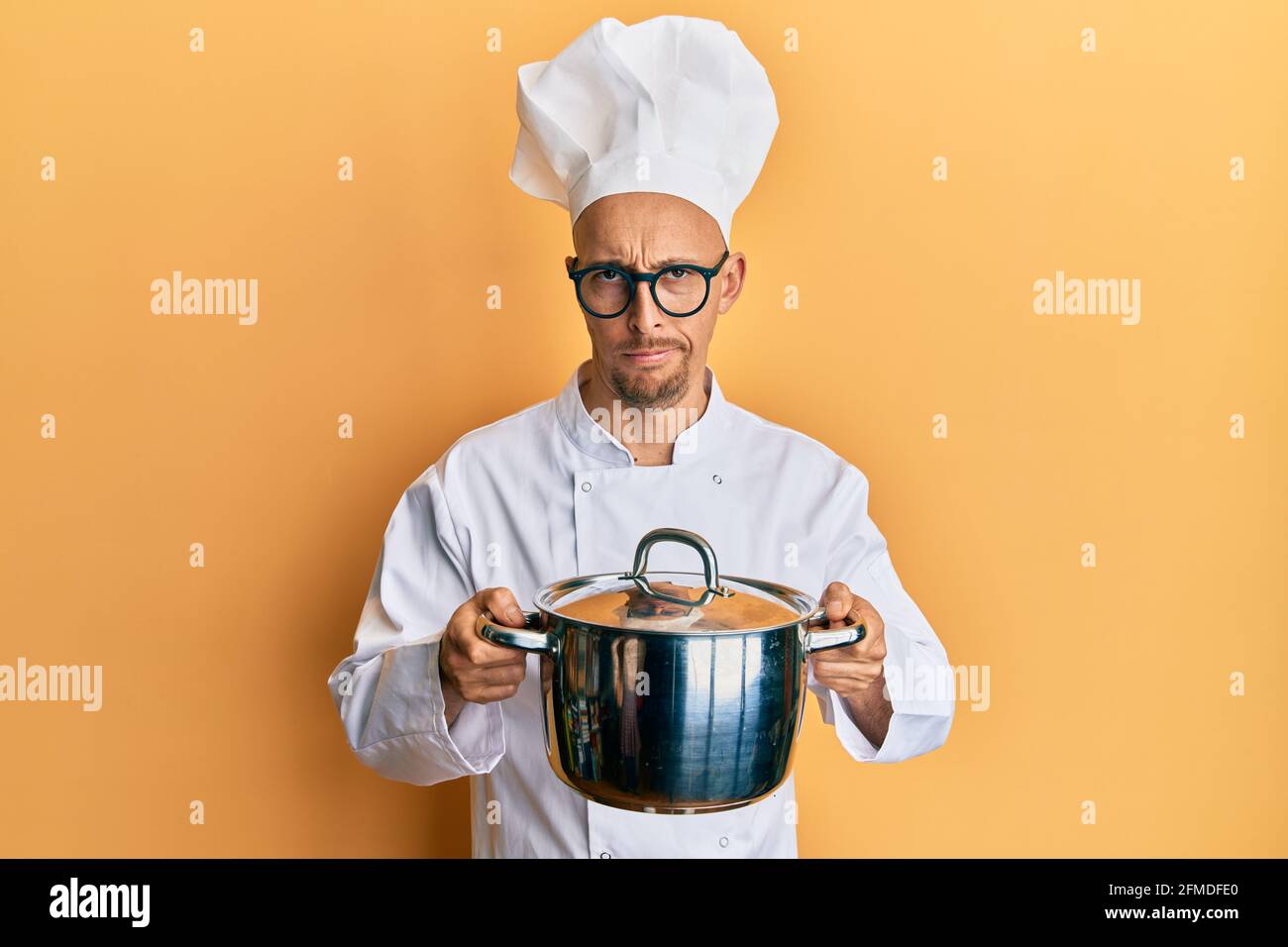 Bald man with beard wearing professional cook holding cooking pot ...