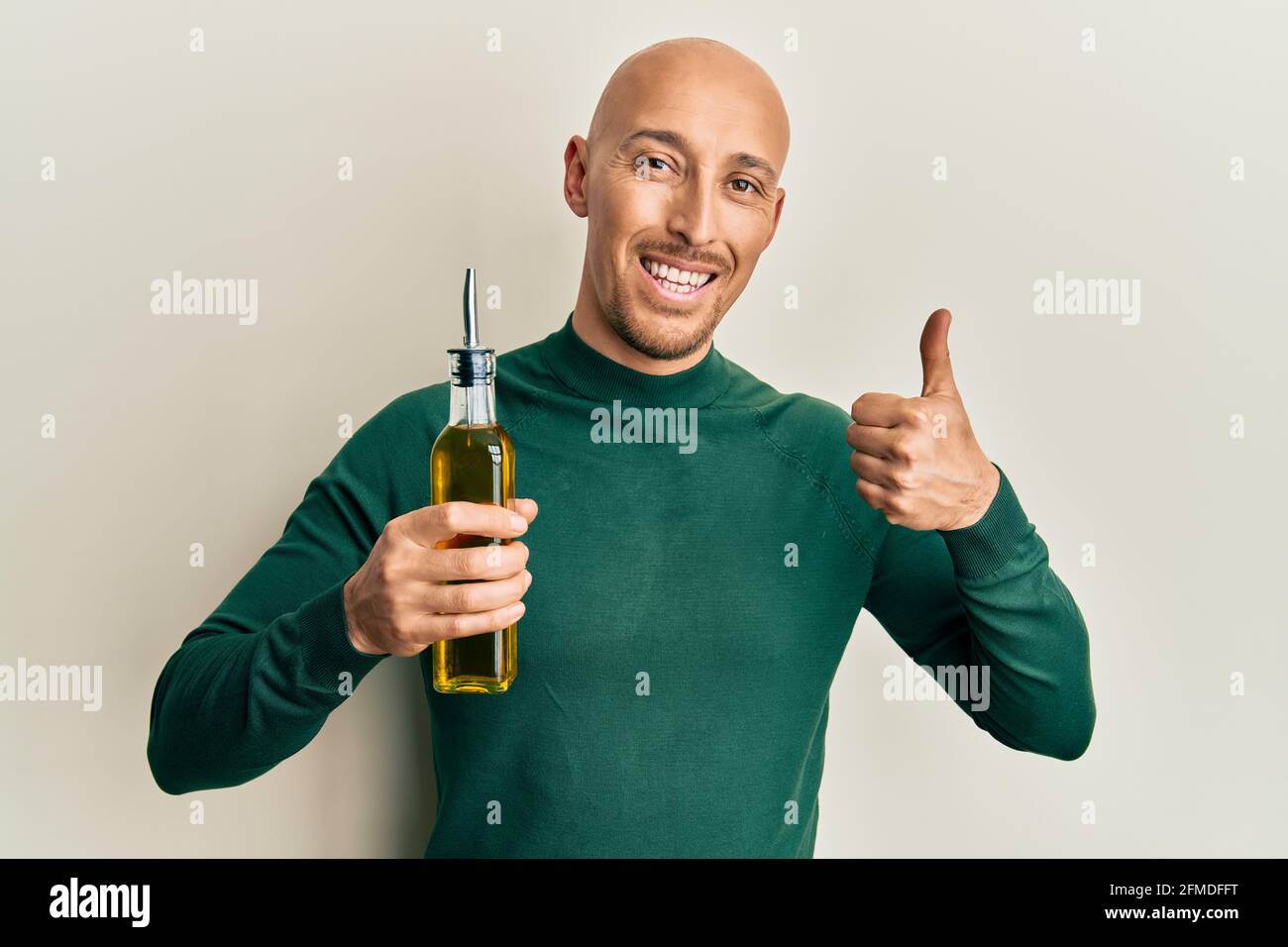 Bald man with beard holding olive oil smiling happy and positive, thumb ...
