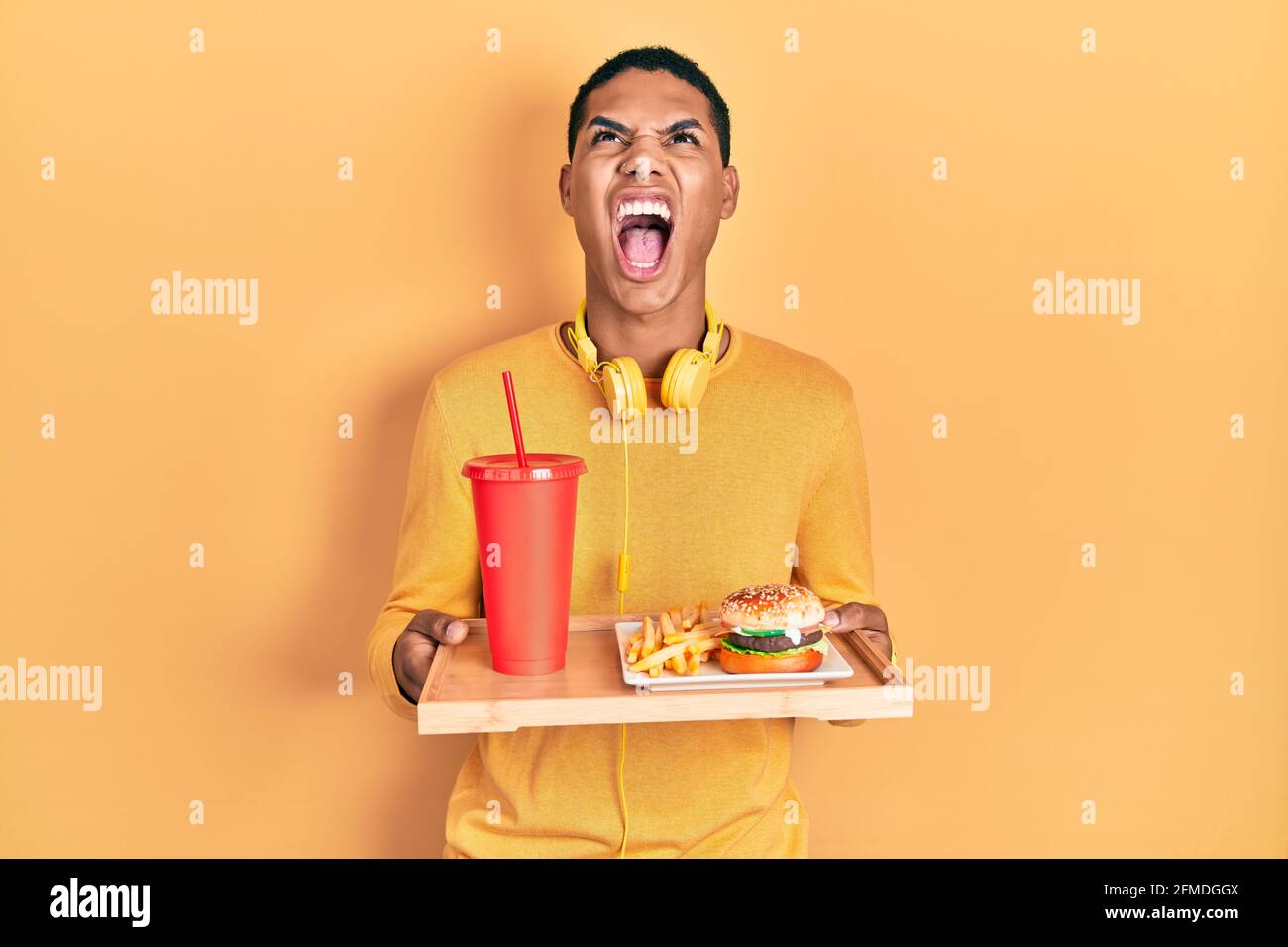 Young african american guy eating a tasty classic burger angry and mad ...