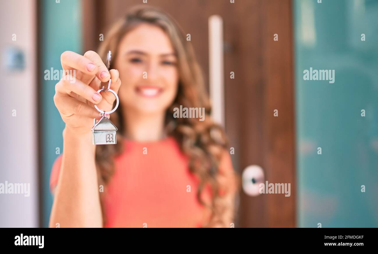 Young blonde girl smiling happy holding key of new house standing at ...