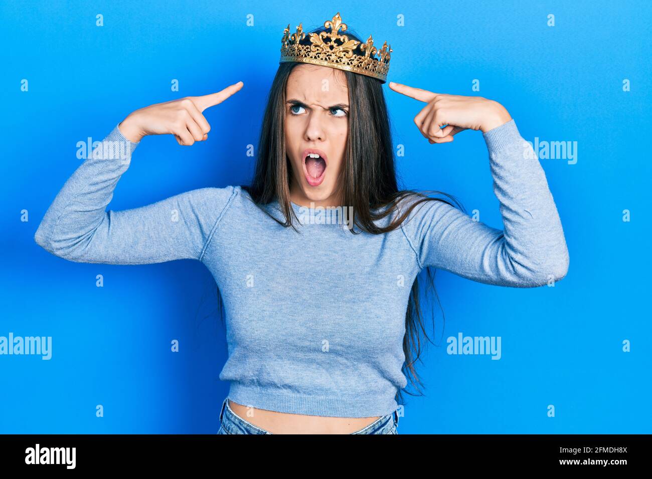 Young brunette teenager wearing princess crown angry and mad screaming ...