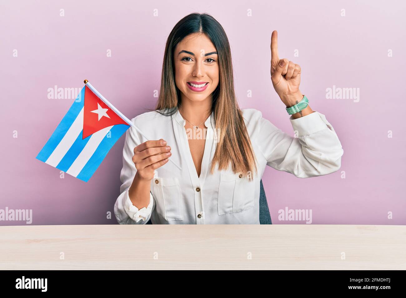 Young hispanic woman holding cuba flag sitting on the table smiling ...