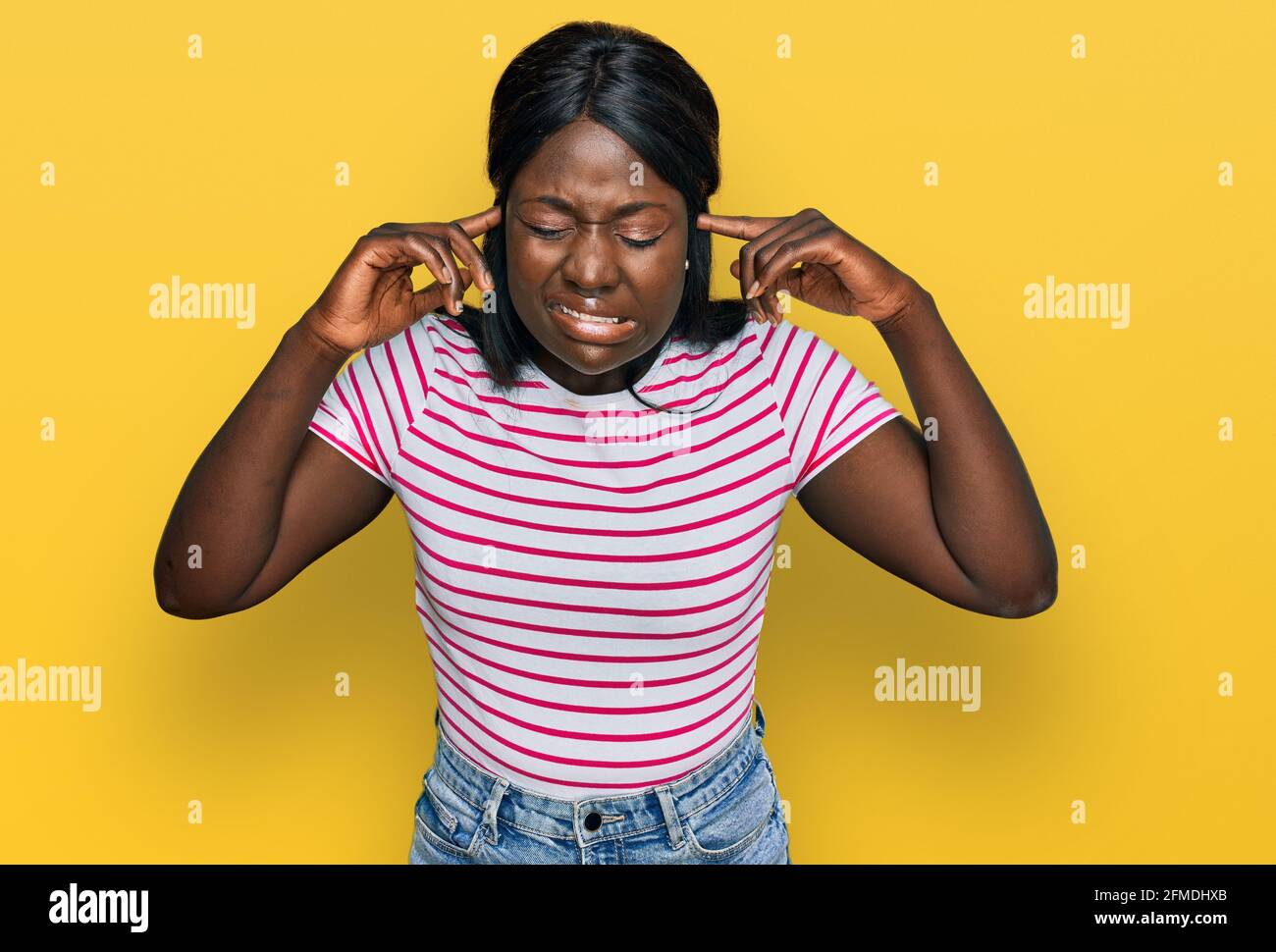African young woman wearing casual striped t shirt covering ears with ...