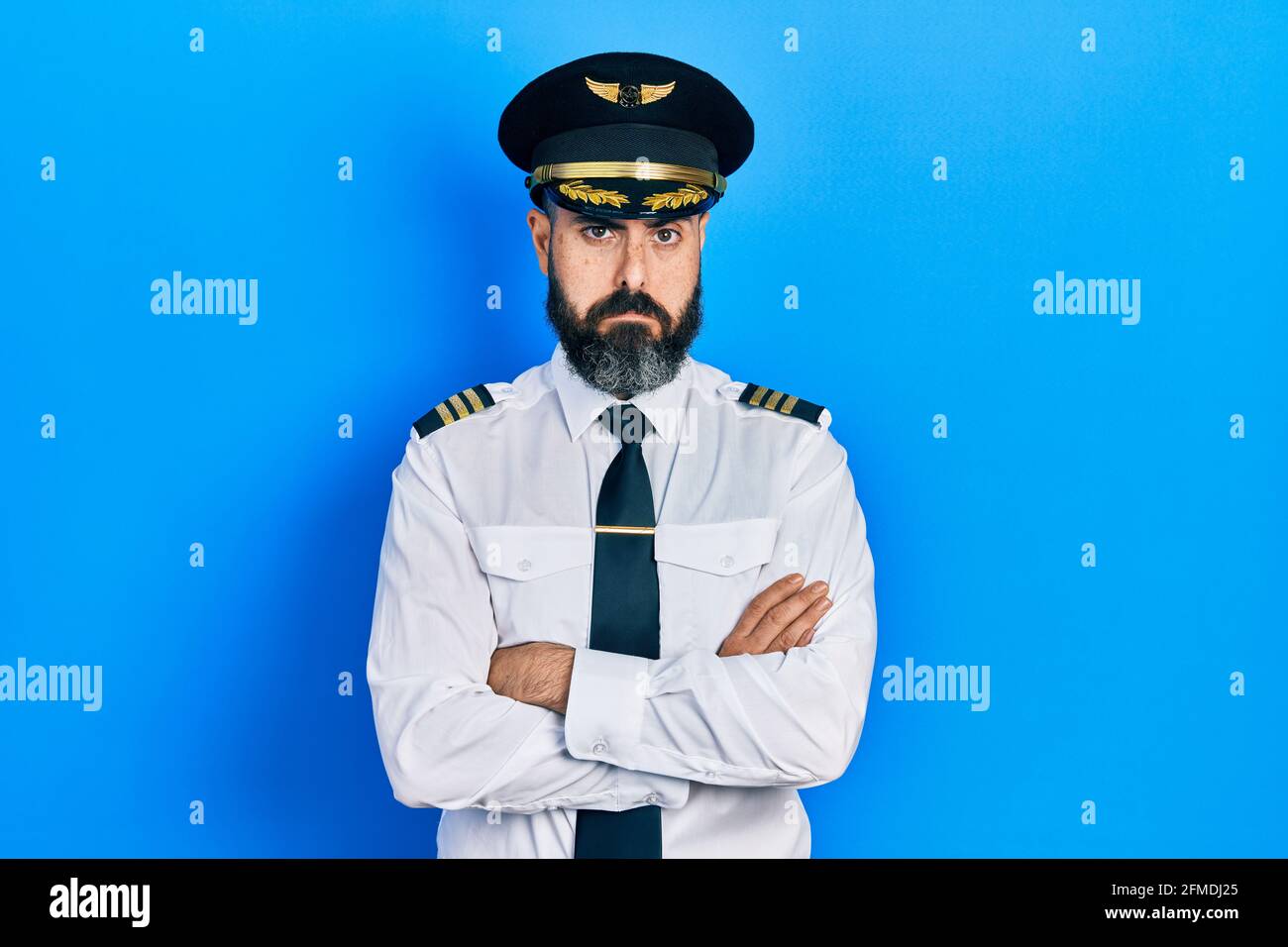 Young hispanic man wearing airplane pilot uniform with arms crossed ...