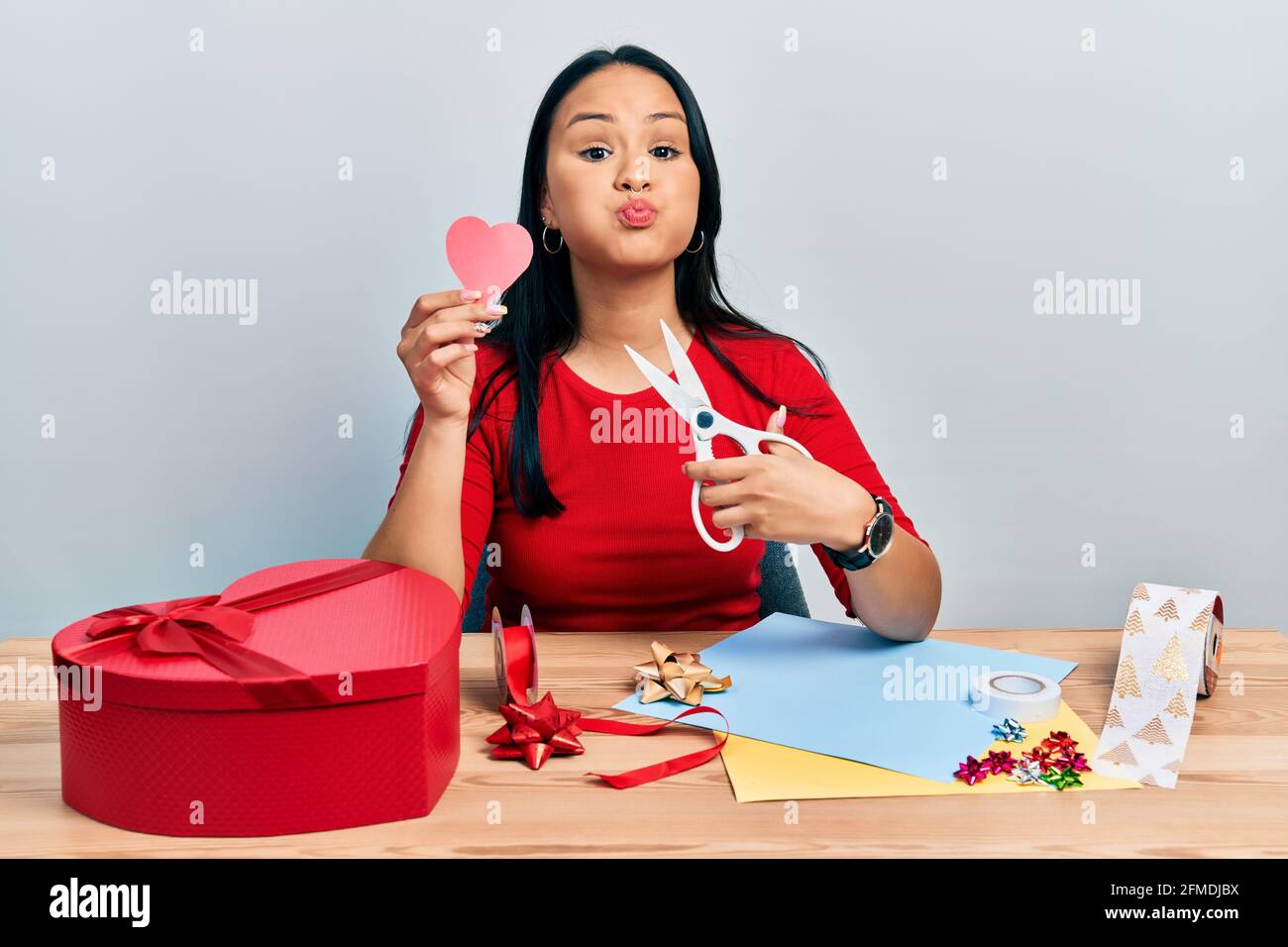 Beautiful hispanic woman with nose piercing doing handcraft heart ...