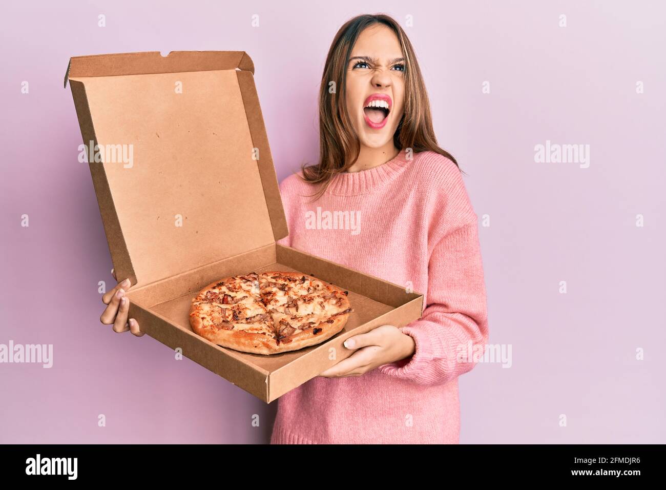 Young brunette woman holding italian pizza angry and mad screaming ...