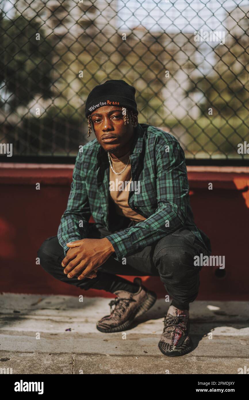 Handsome and stylish Spanish man posing while crouching on a chain-link ...