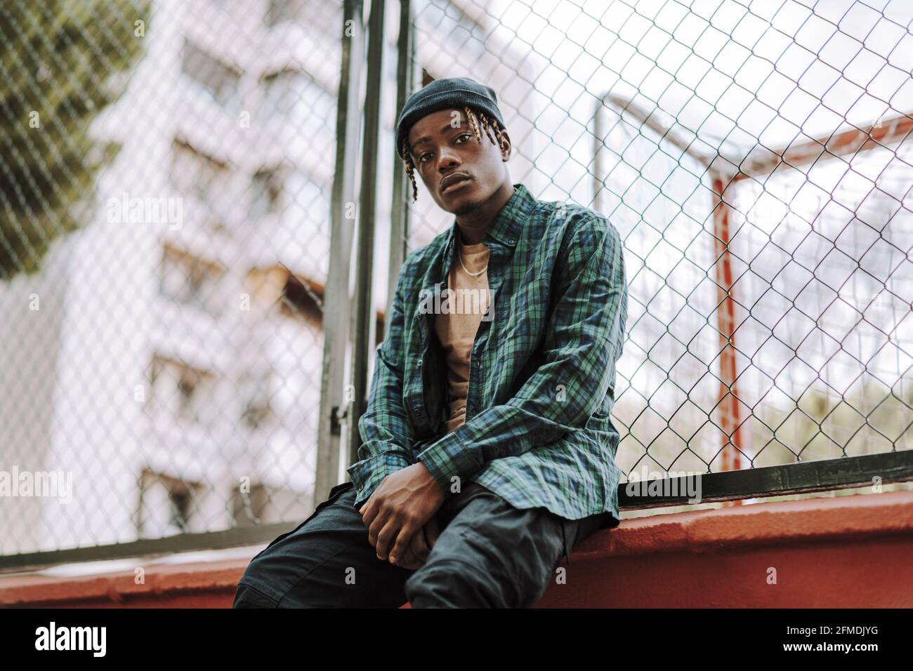 Handsome and stylish Spanish man posing on a chain-link fence ...