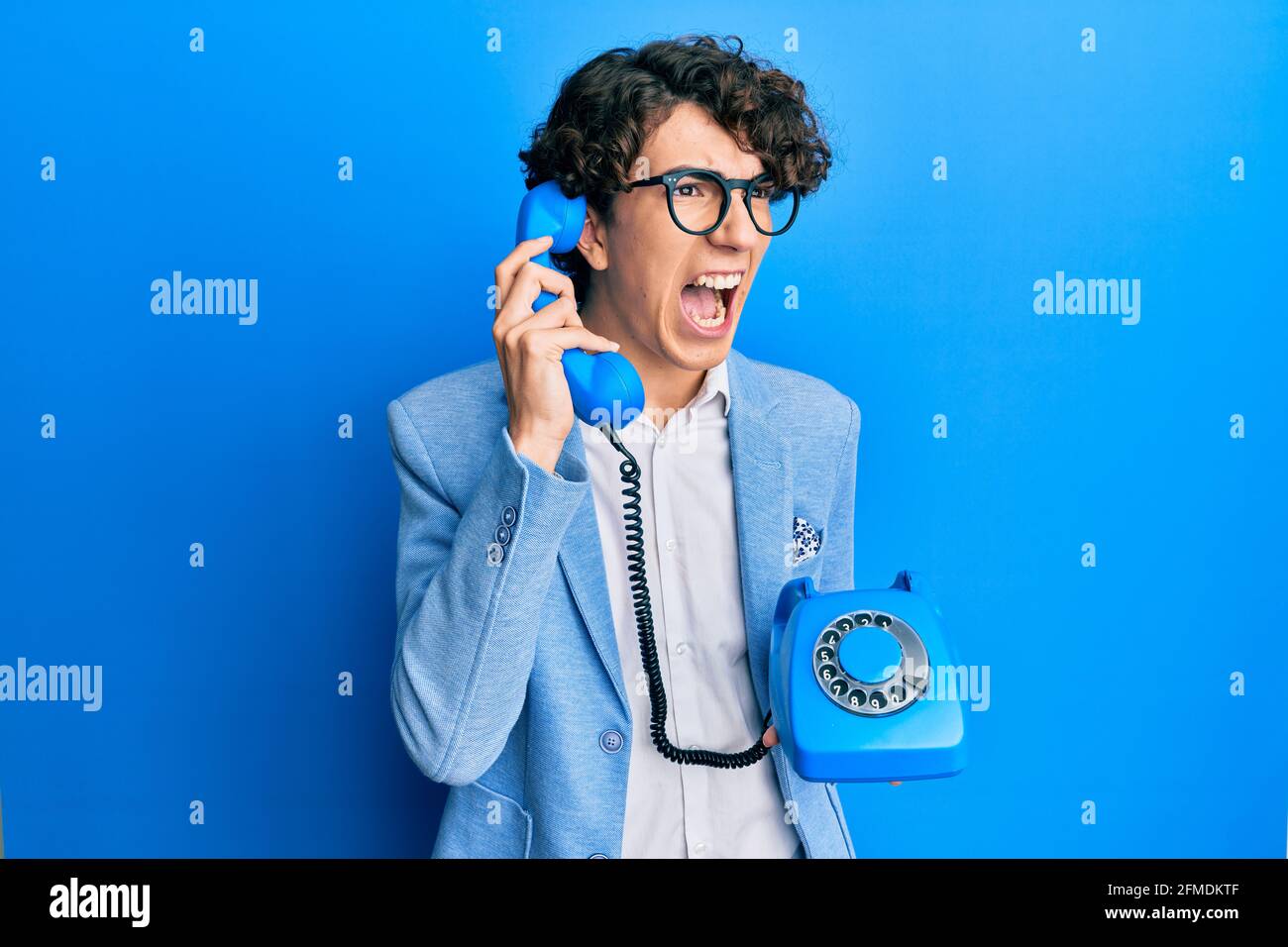Hispanic young man speaking on vintage telephone angry and mad ...