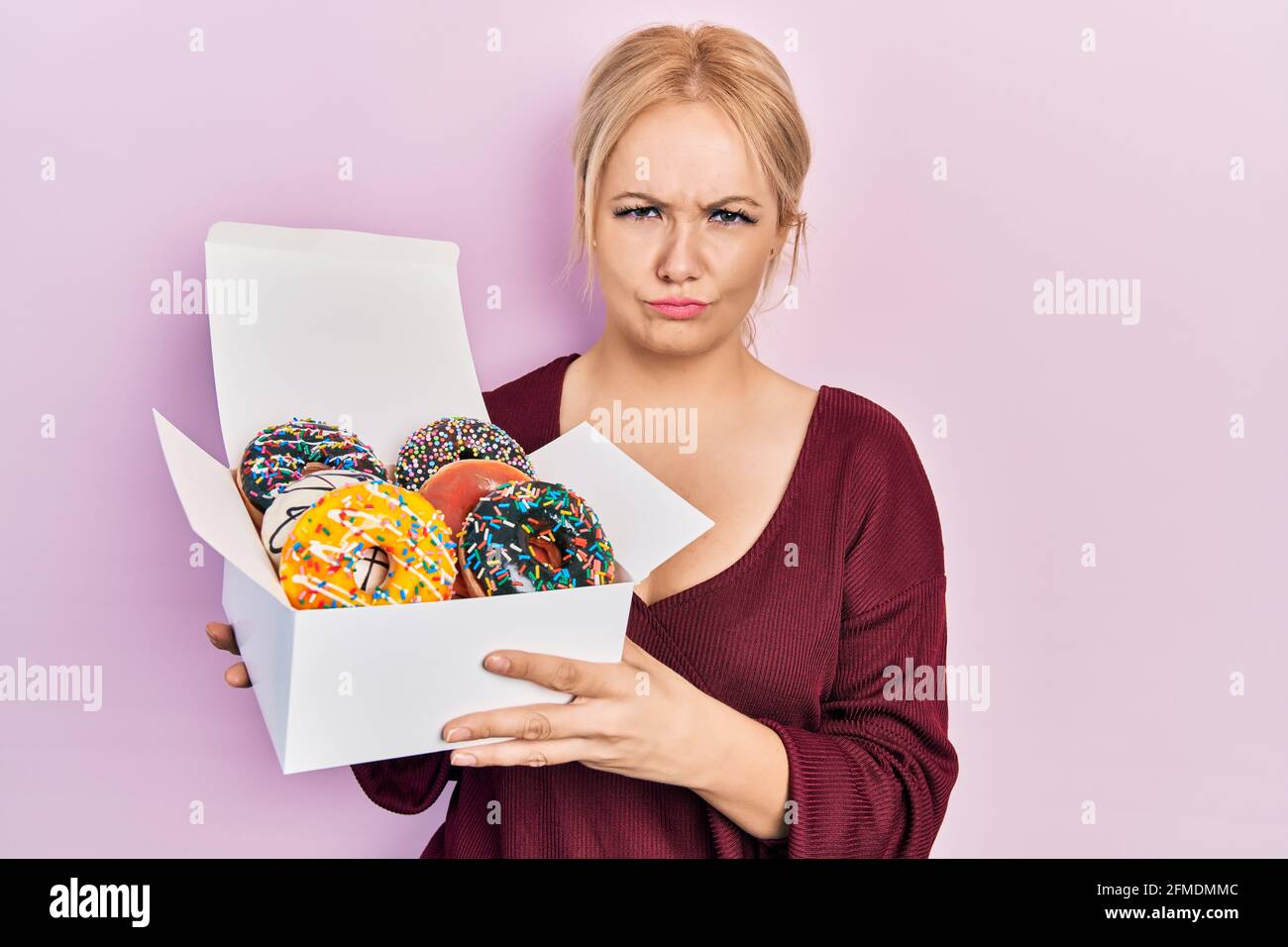 Young blonde woman holding tasty colorful doughnuts depressed and worry ...