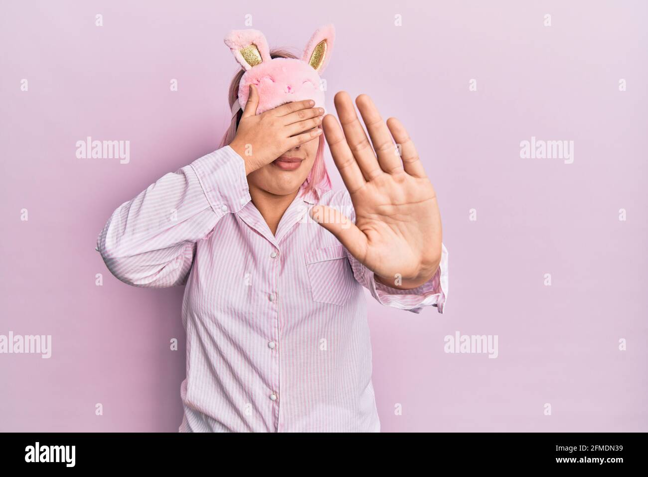 Hispanic woman with pink hair wearing sleep mask and pajama covering ...