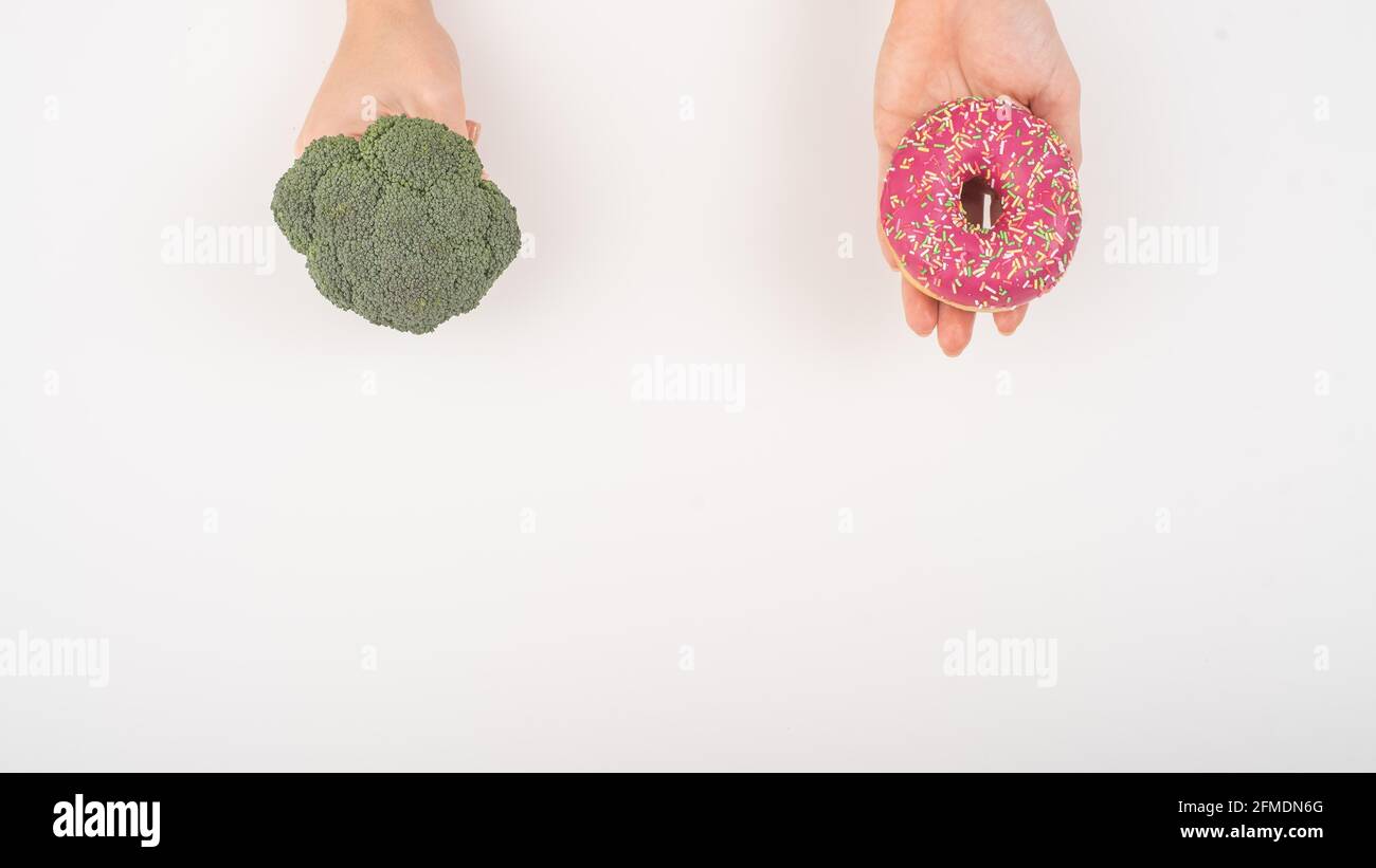 Comparison of eating habits. Woman holding broccoli and donut on a ...