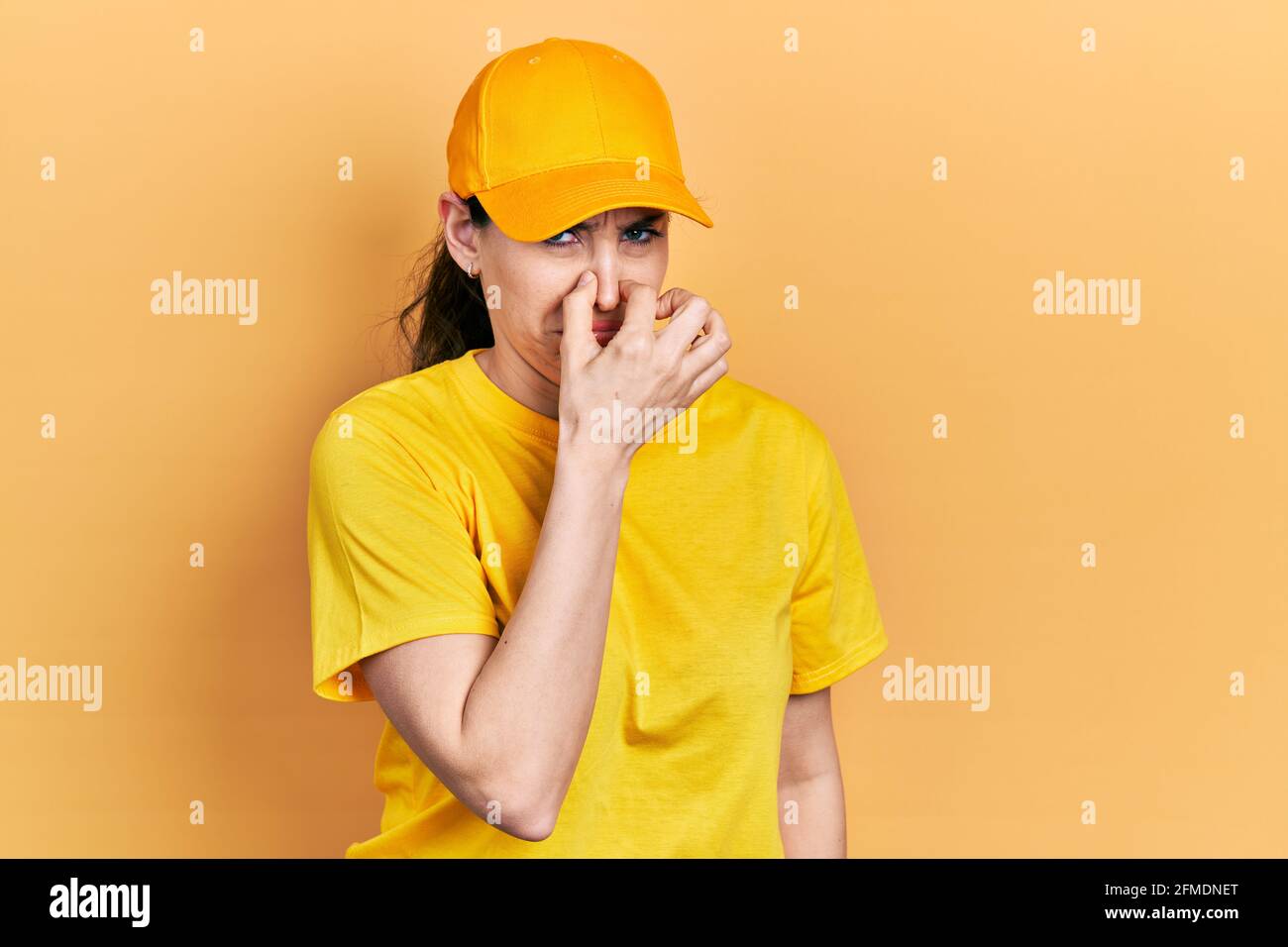 Young hispanic woman wearing delivery uniform and cap smelling ...