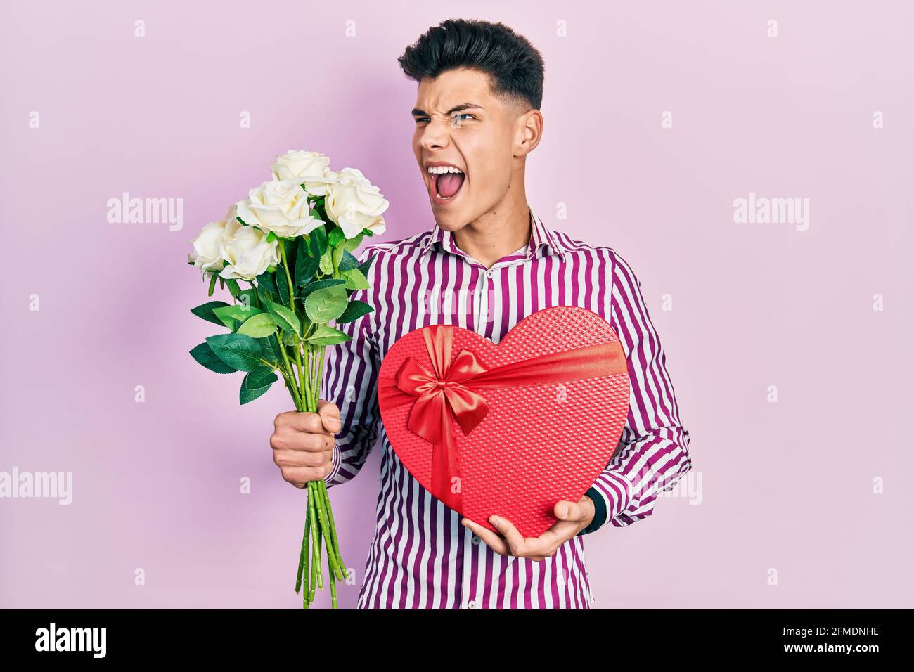 Young hispanic man holding anniversary present and bouquet of flowers ...