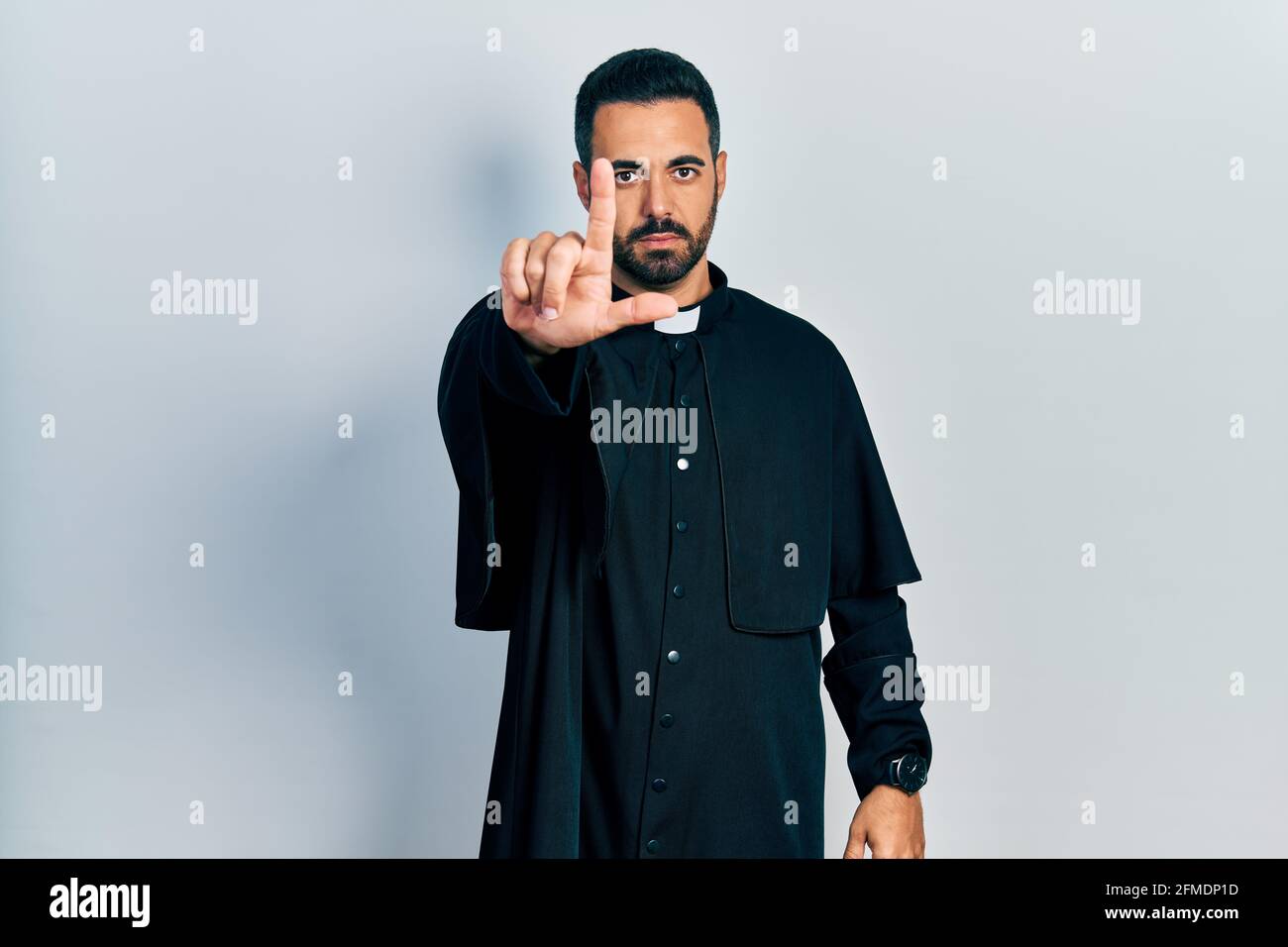 Handsome hispanic man with beard wearing catholic priest robe pointing ...