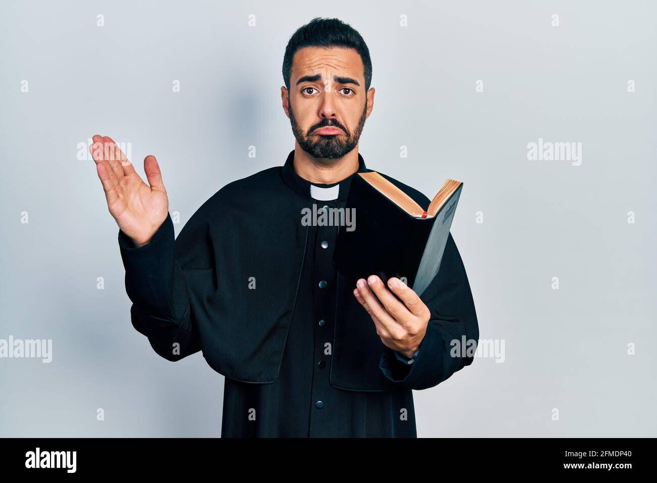 Handsome hispanic priest man with beard holding bible and christian ...