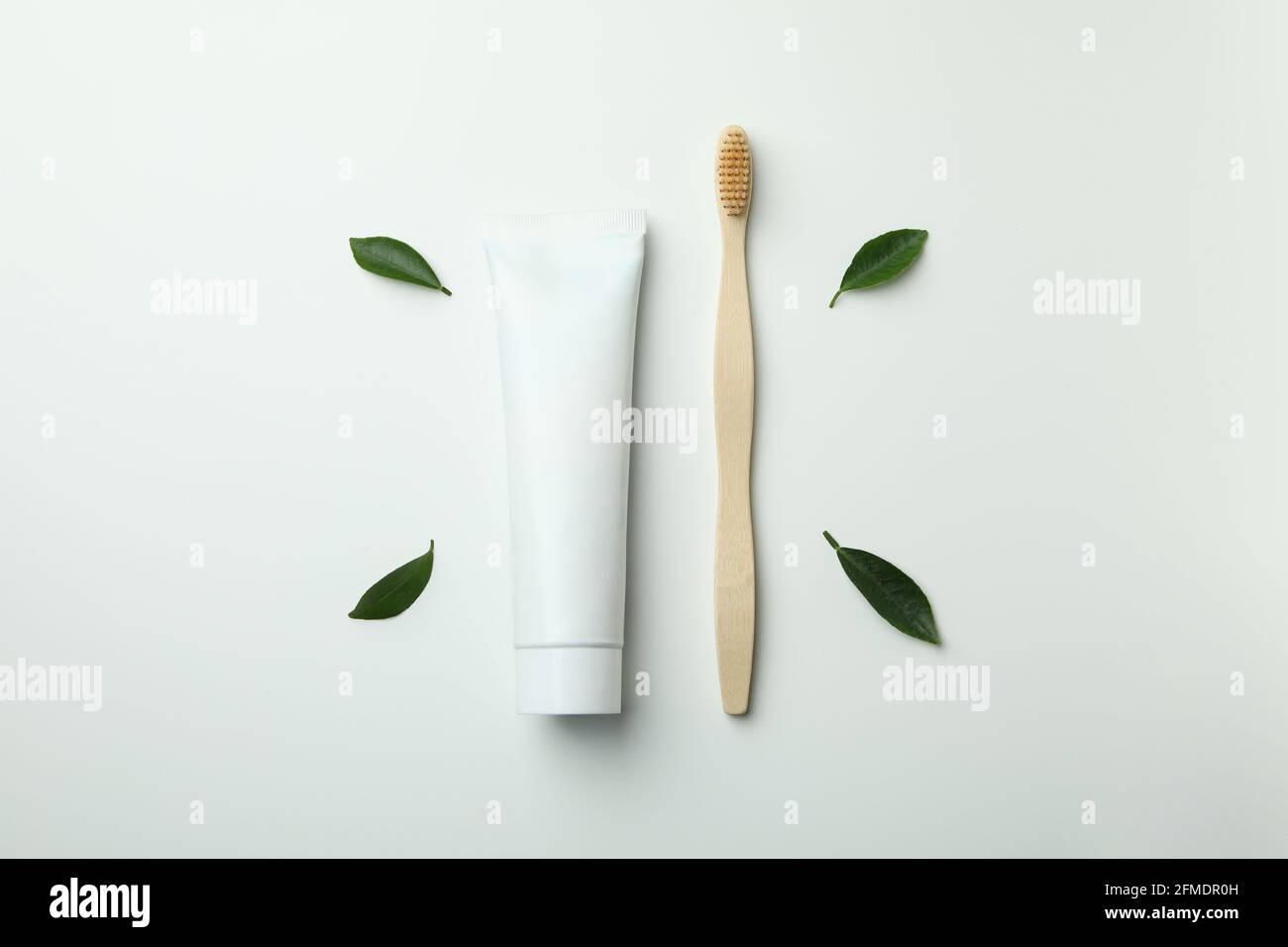 Eco friendly toothbrush, tube of toothpaste and leaves on white ...