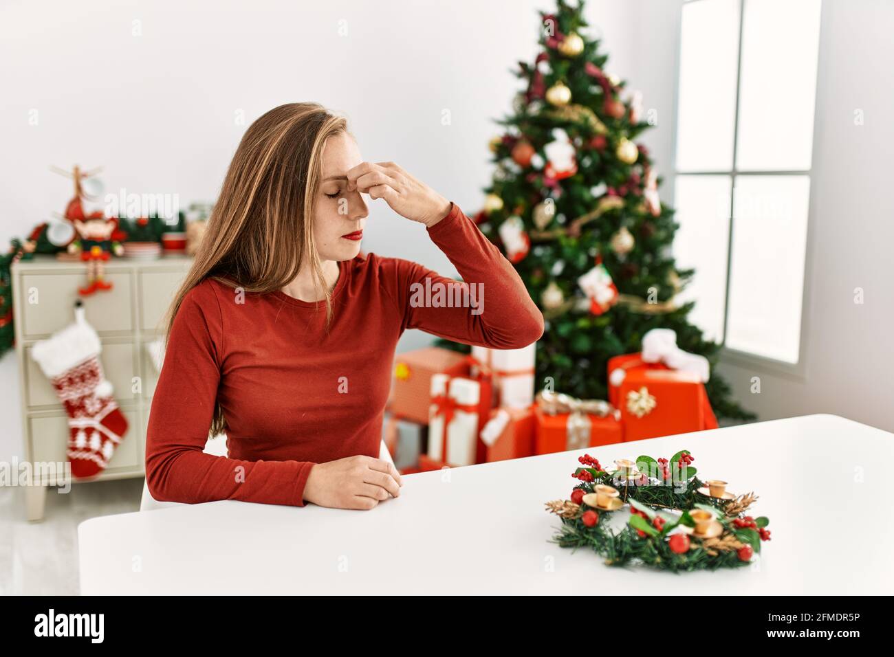 Caucasian young blonde woman sitting on the table by christmas tree ...
