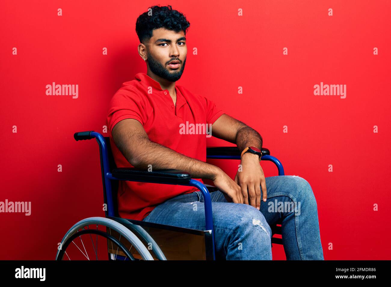 Arab man with beard sitting on wheelchair in shock face, looking ...