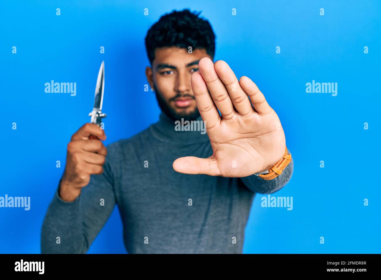 Arab man with beard holding pocket knife with open hand doing stop sign ...
