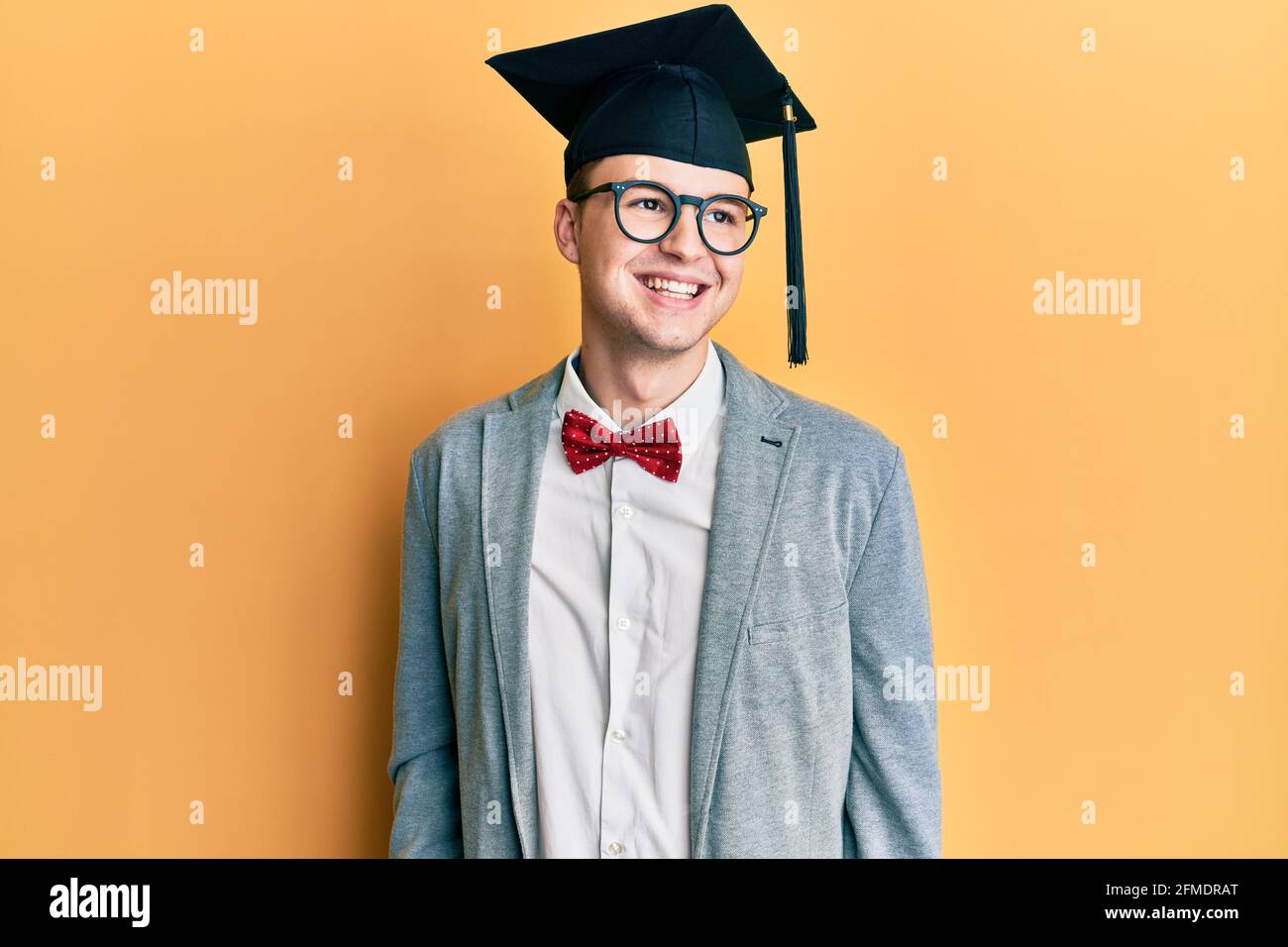 Young caucasian nerd man wearing glasses and graduation cap looking to ...