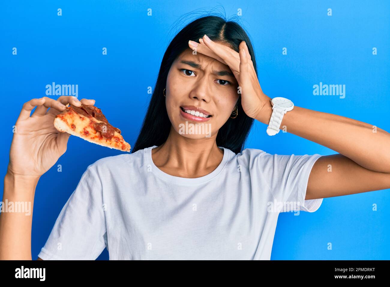 Young chinese woman eating tasty pepperoni pizza stressed and ...