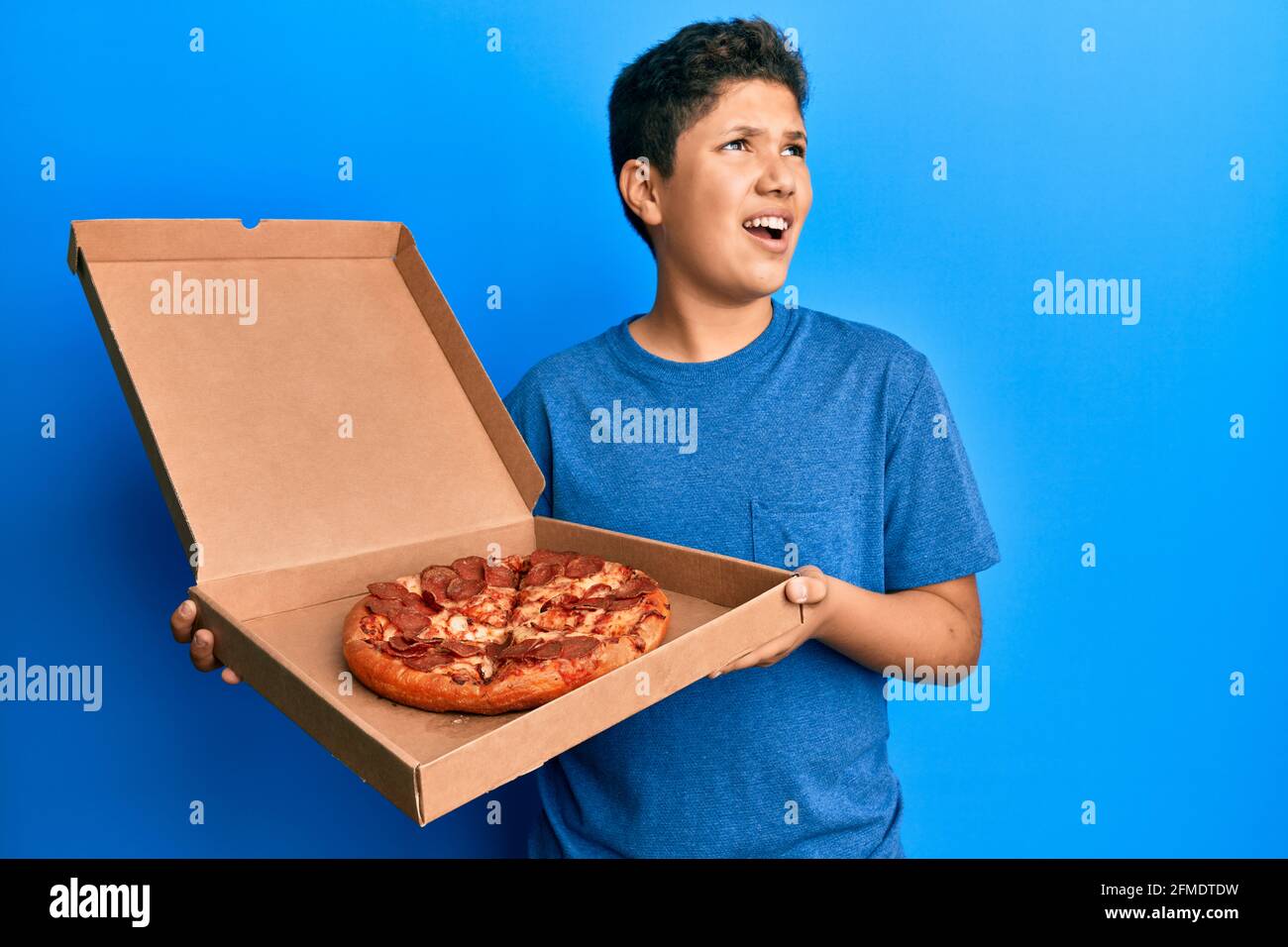 Teenager hispanic boy eating tasty pepperoni pizza angry and mad ...