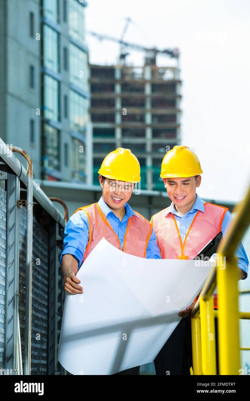 Asian Indonesian construction workers with blueprint or plan on ...